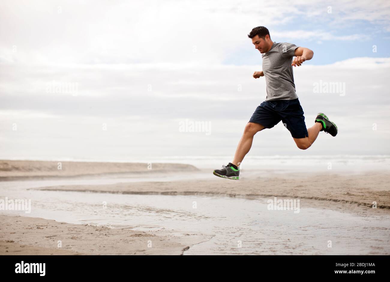 Young man jumping over shallow water on a beach Stock Photo - Alamy