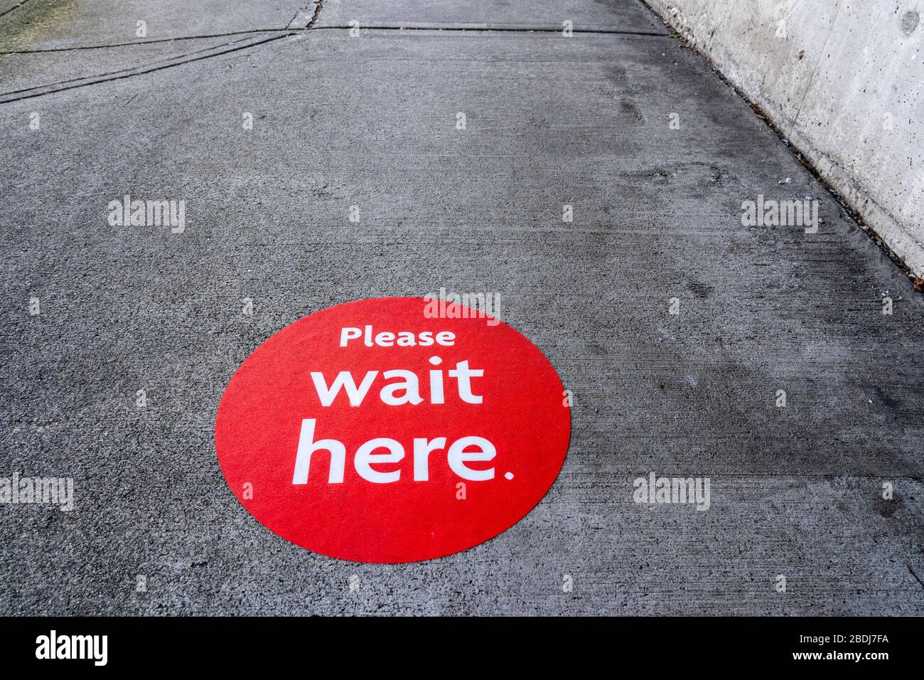 Round red physical distancing notification with words "Please Wait Here ...