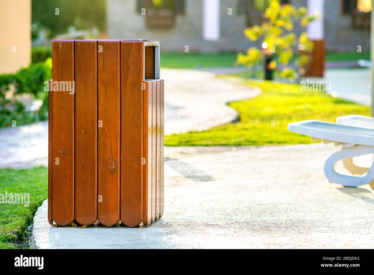 Yellow wooden trash can outdoors on the side of sidewalk in park ...