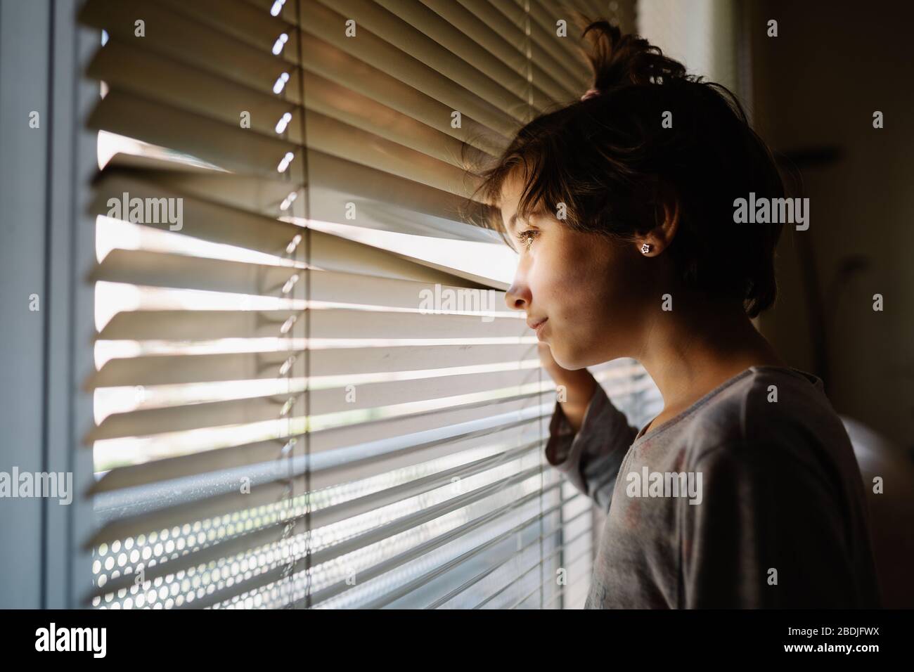 Nine-years-old girl looking out the window through the blinds in the ...