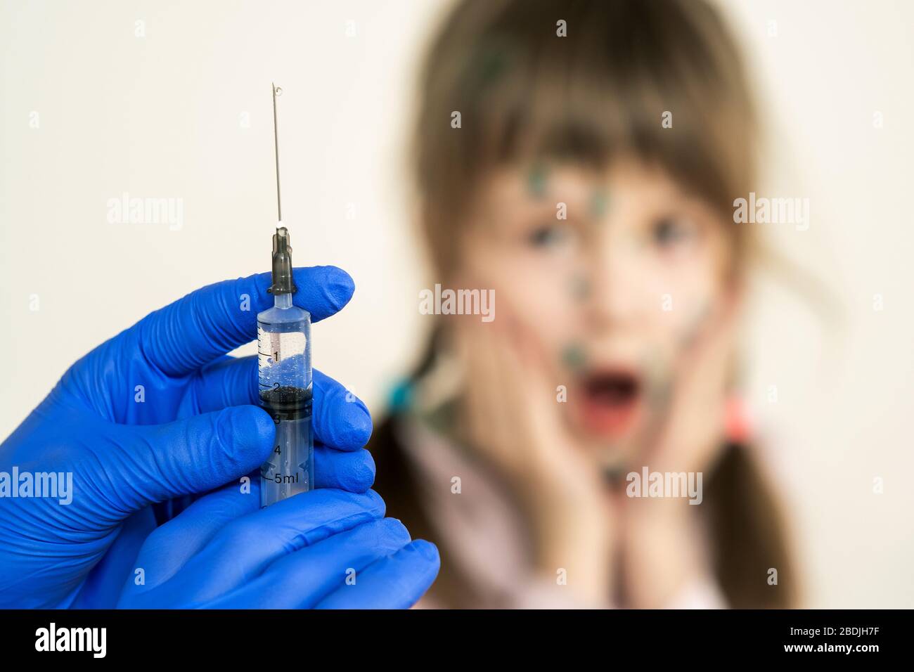 Doctor preparing vaccination injection with a syringe to an afraid ...