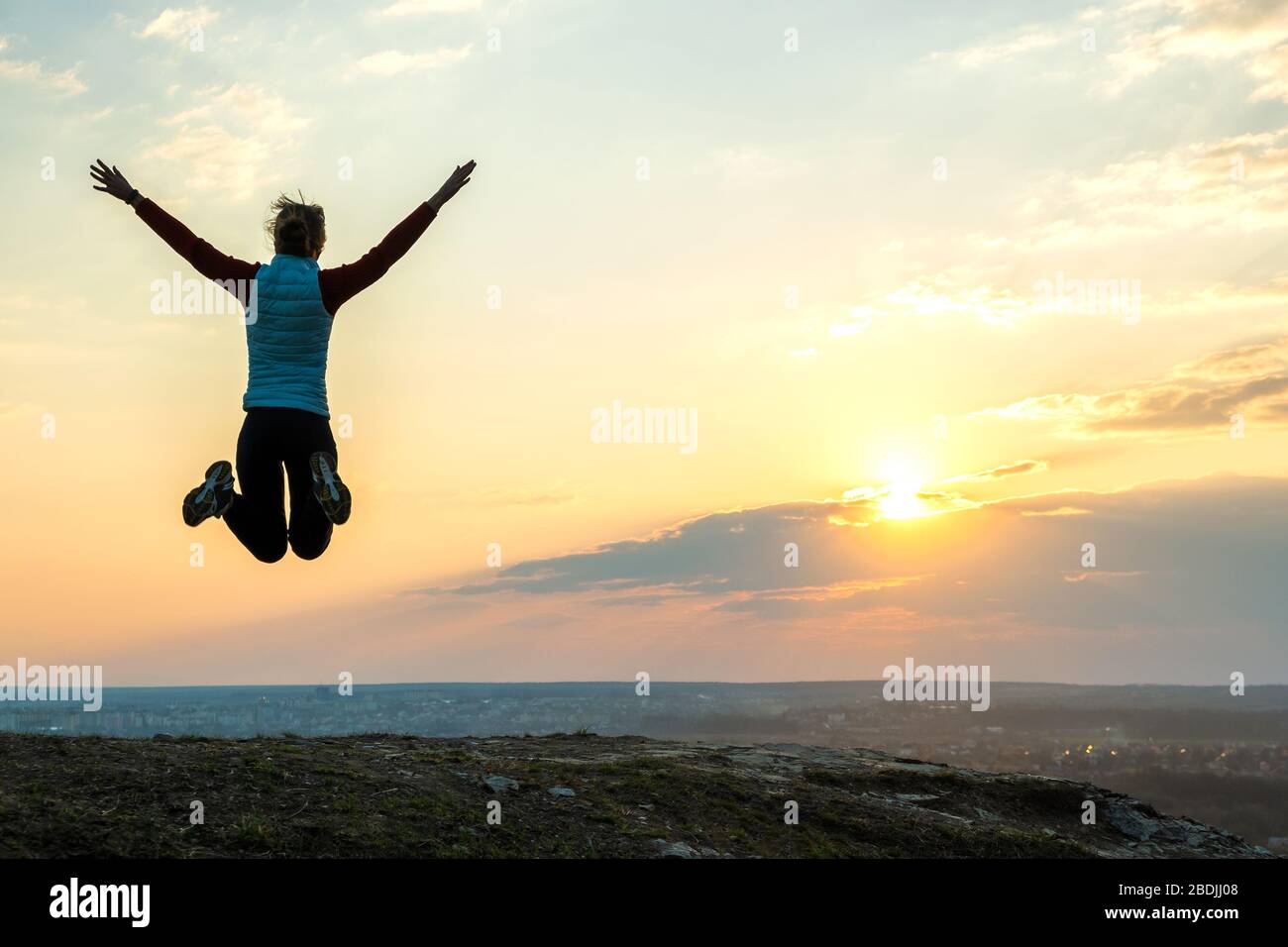 Silhouette of a woman hiker jumping alone on empty field at sunset in ...