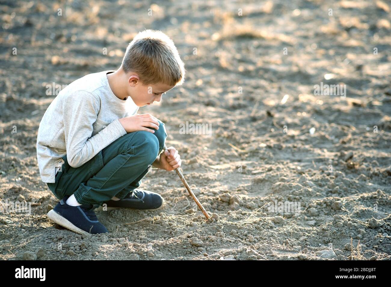 Child boy playing with wooden stick digging in black dirt ground ...