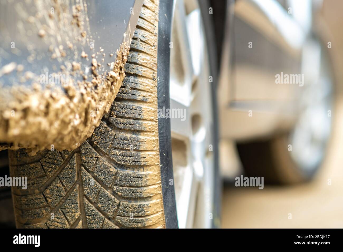 Close up of dirty car wheel with rubber tire covered with yellow mud ...