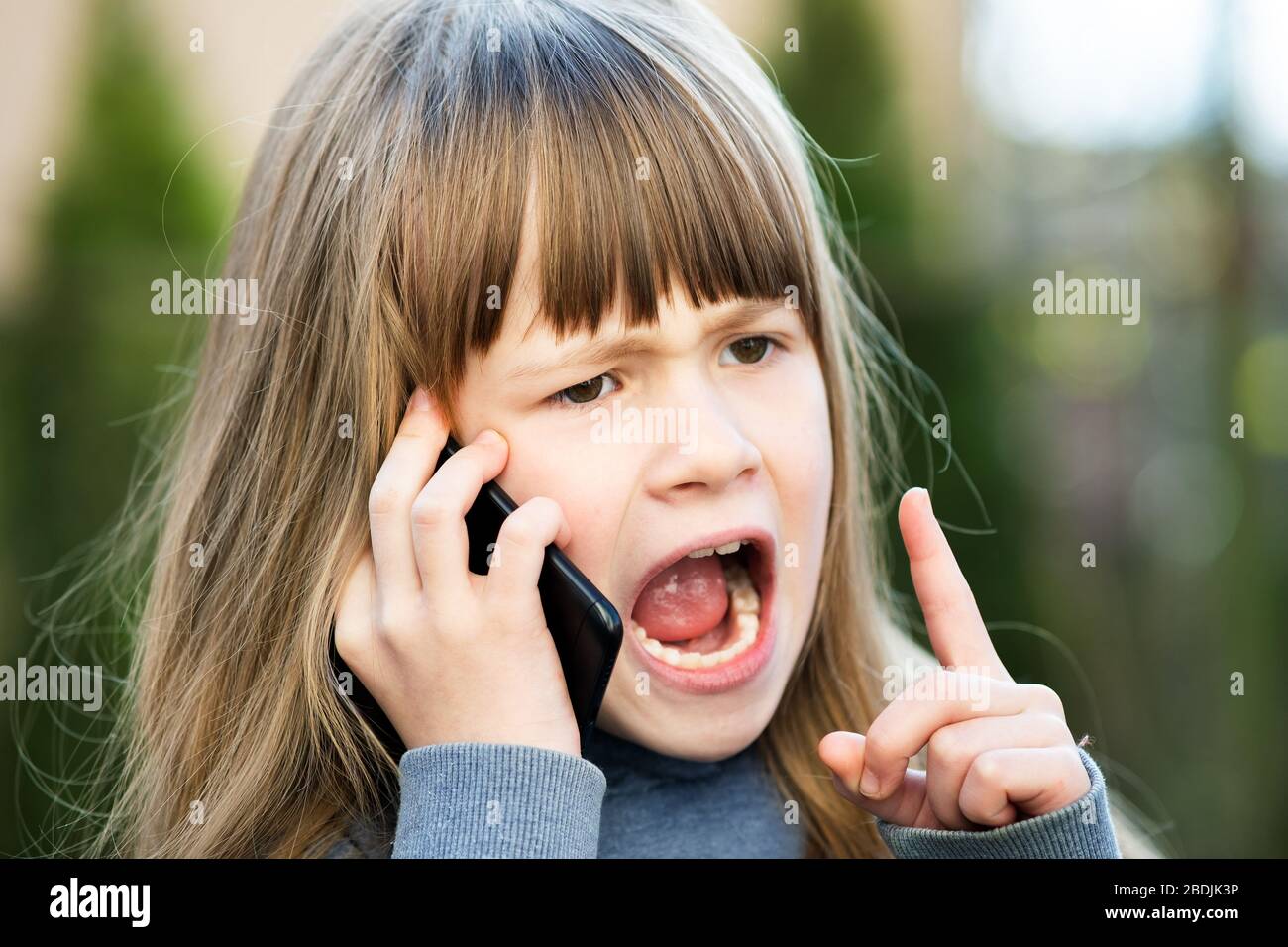 Portrait of angry child girl with long hair talking on cell phone ...