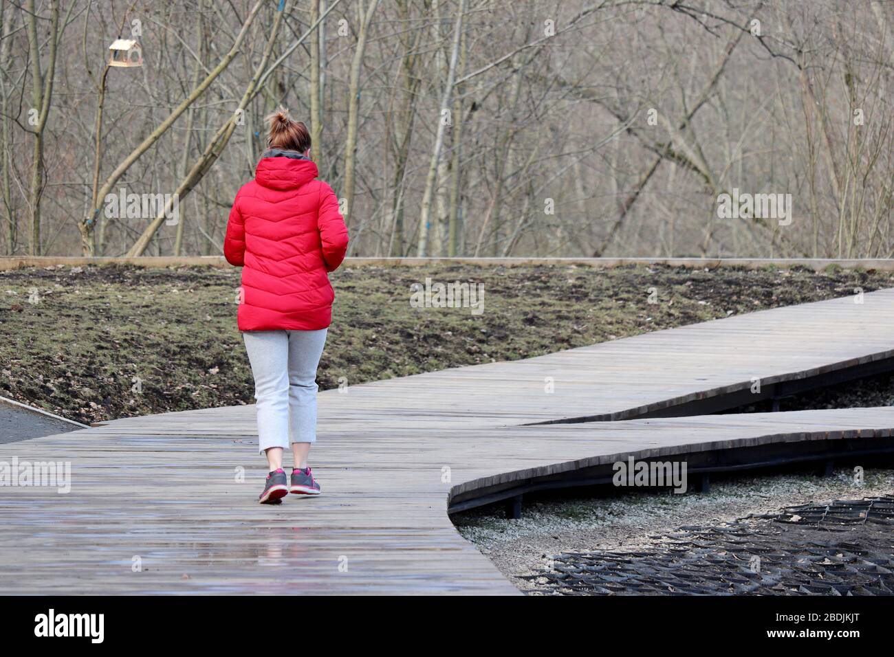 Girl in red down jacket running in the spring park, rear view. Concept ...