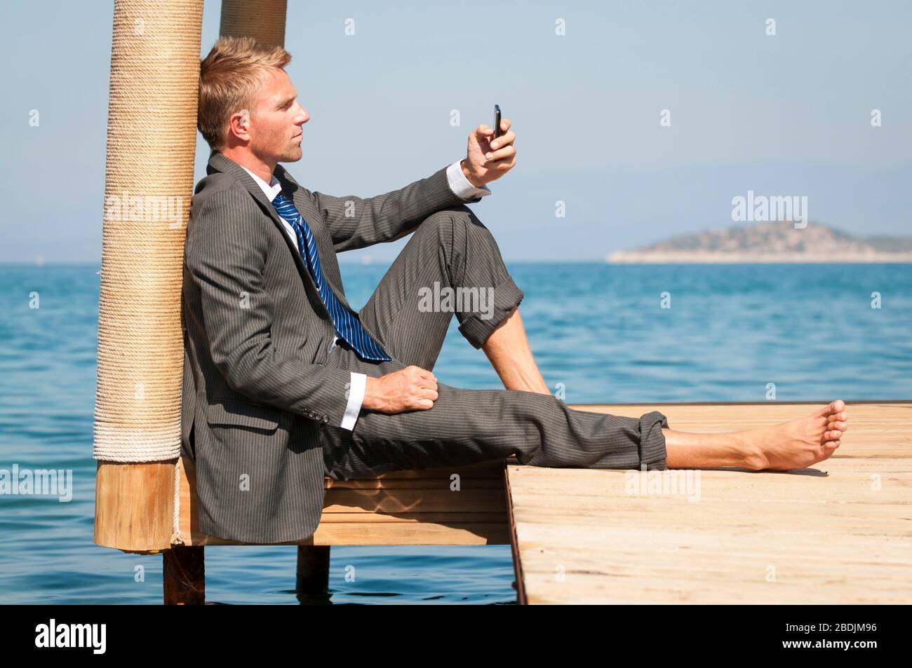 Barefoot businessman relaxing with his smartphone sitting outdoors on a ...