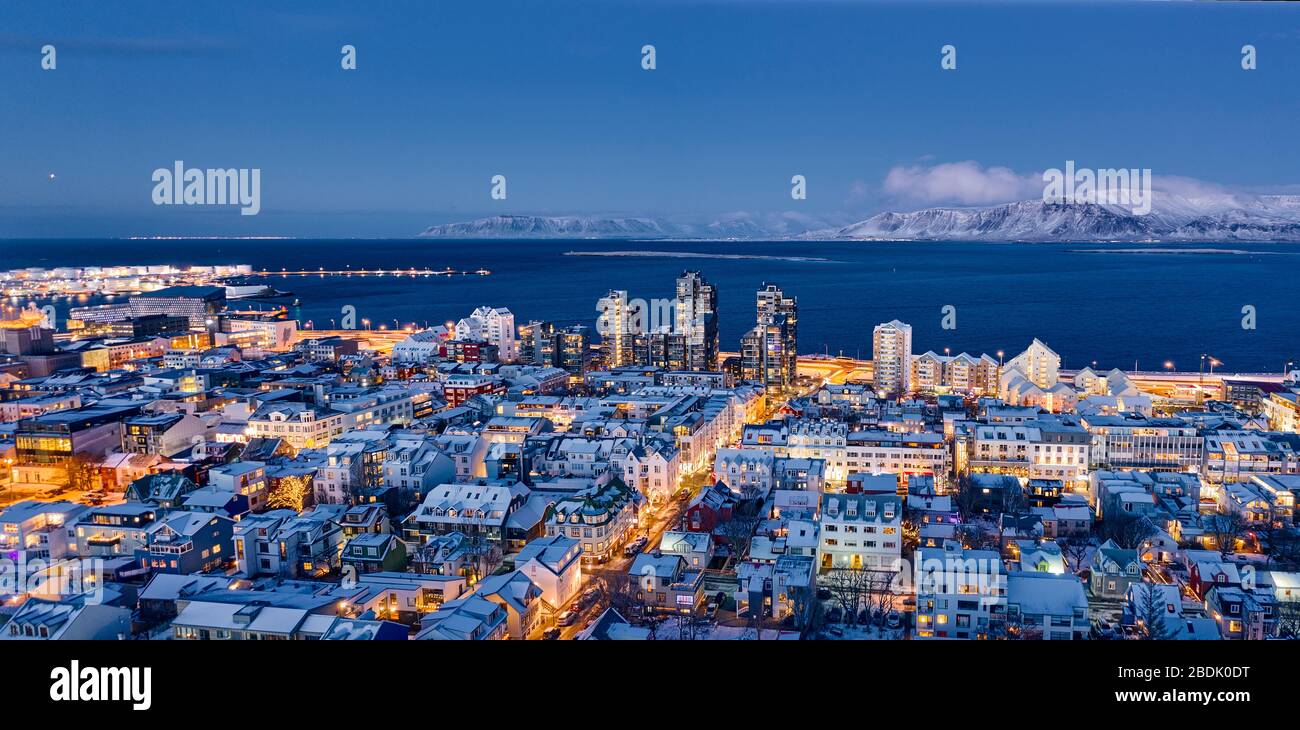 Aerial view of illuminated city on ocean coast with snowy mountains on ...