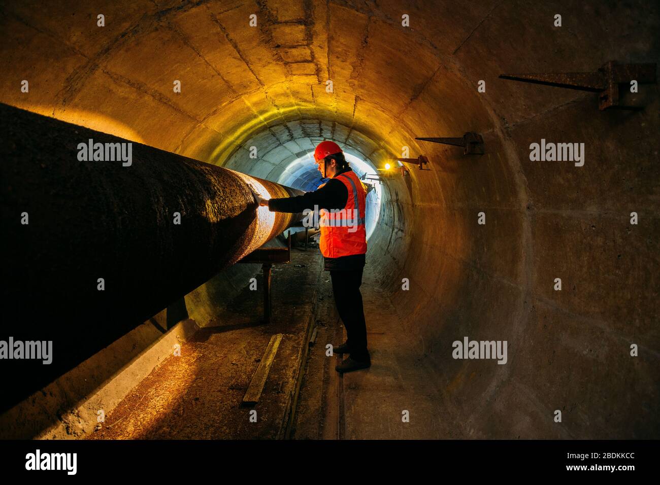 Tunnel worker examines pipeline in underground tunnel Stock Photo - Alamy