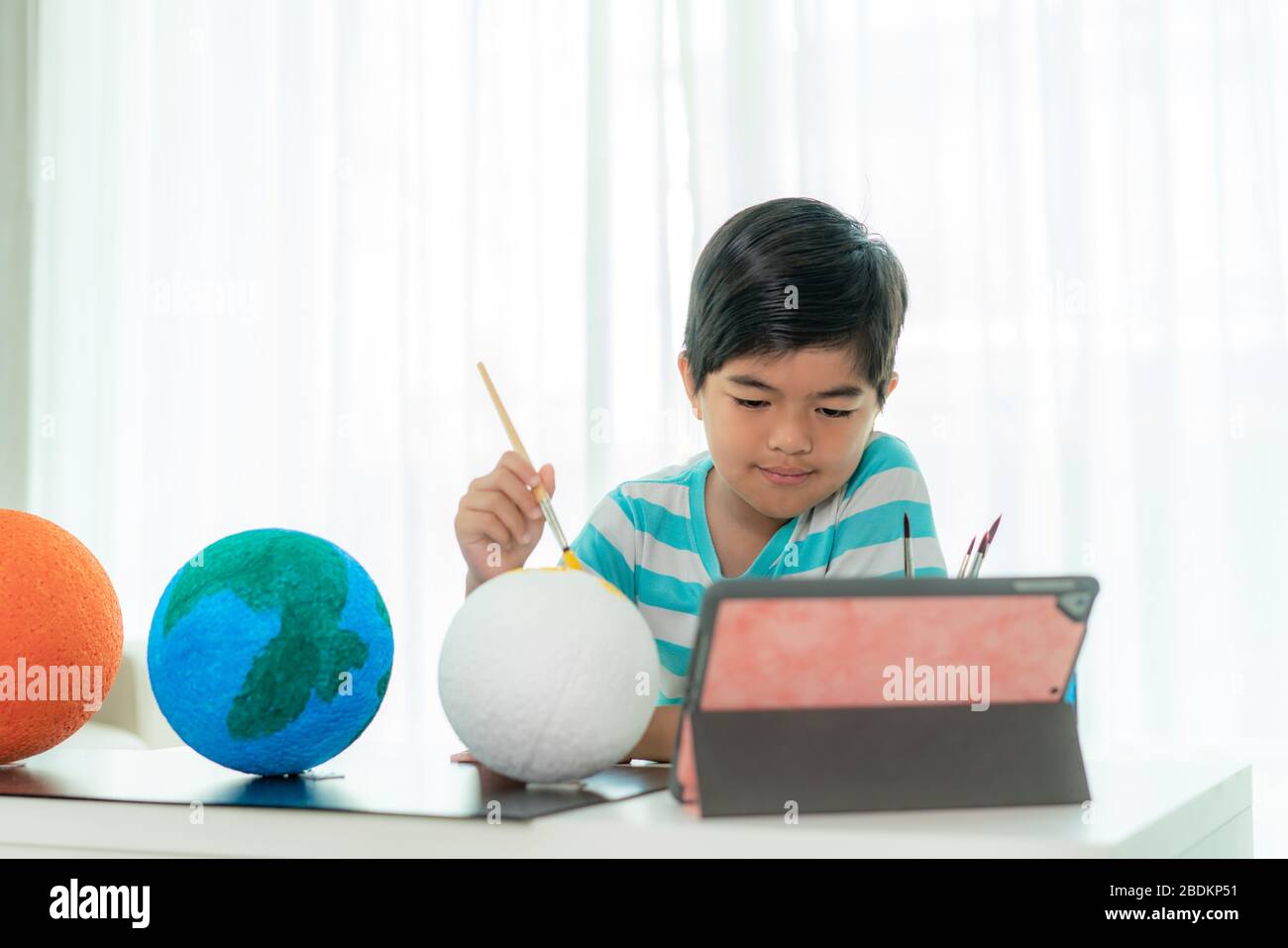 Asian elementary schoolboy painting the moon in science class learning ...