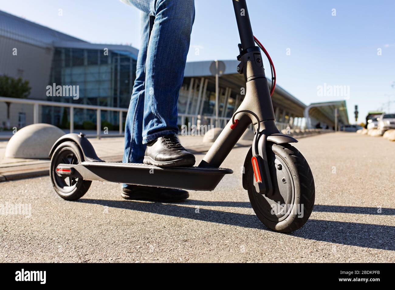 Legs of a man standing on e-scooter parked on sidewalk at cityscape on ...