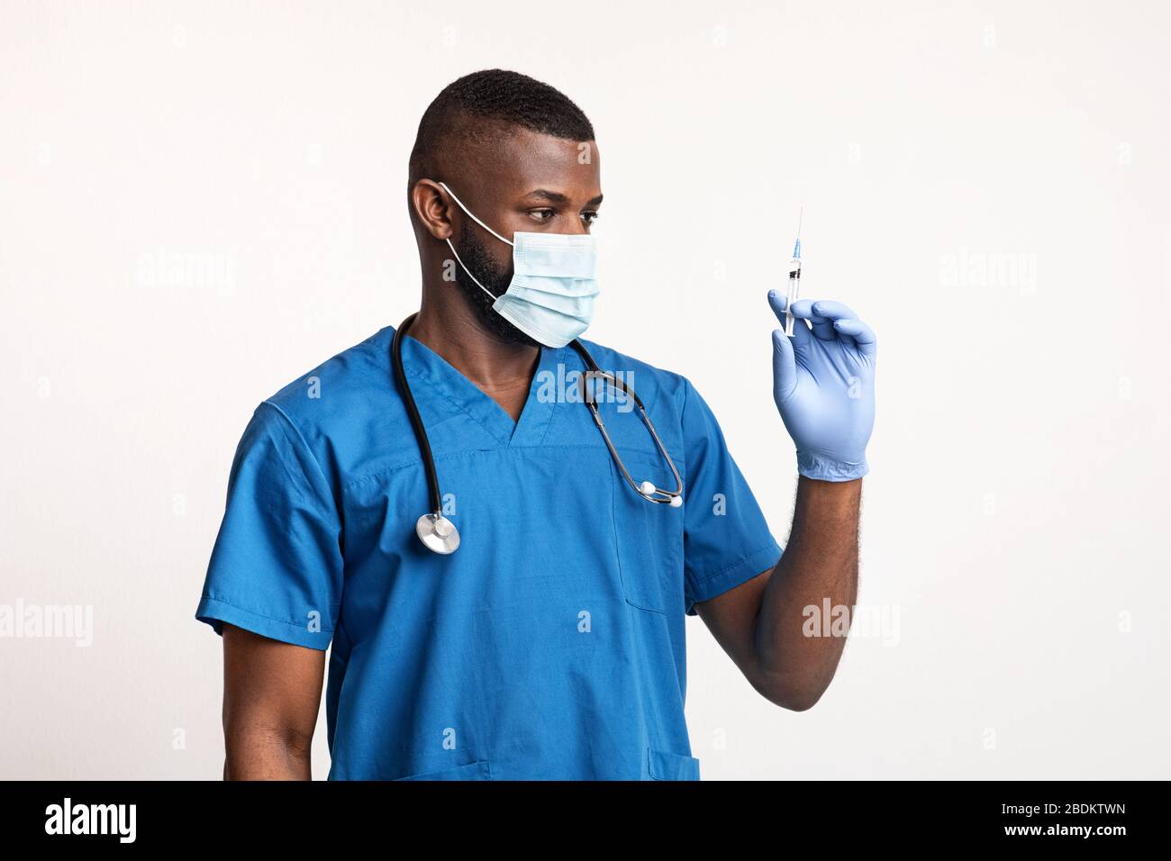 African doc in face mask and gloves looking at syringe Stock Photo - Alamy