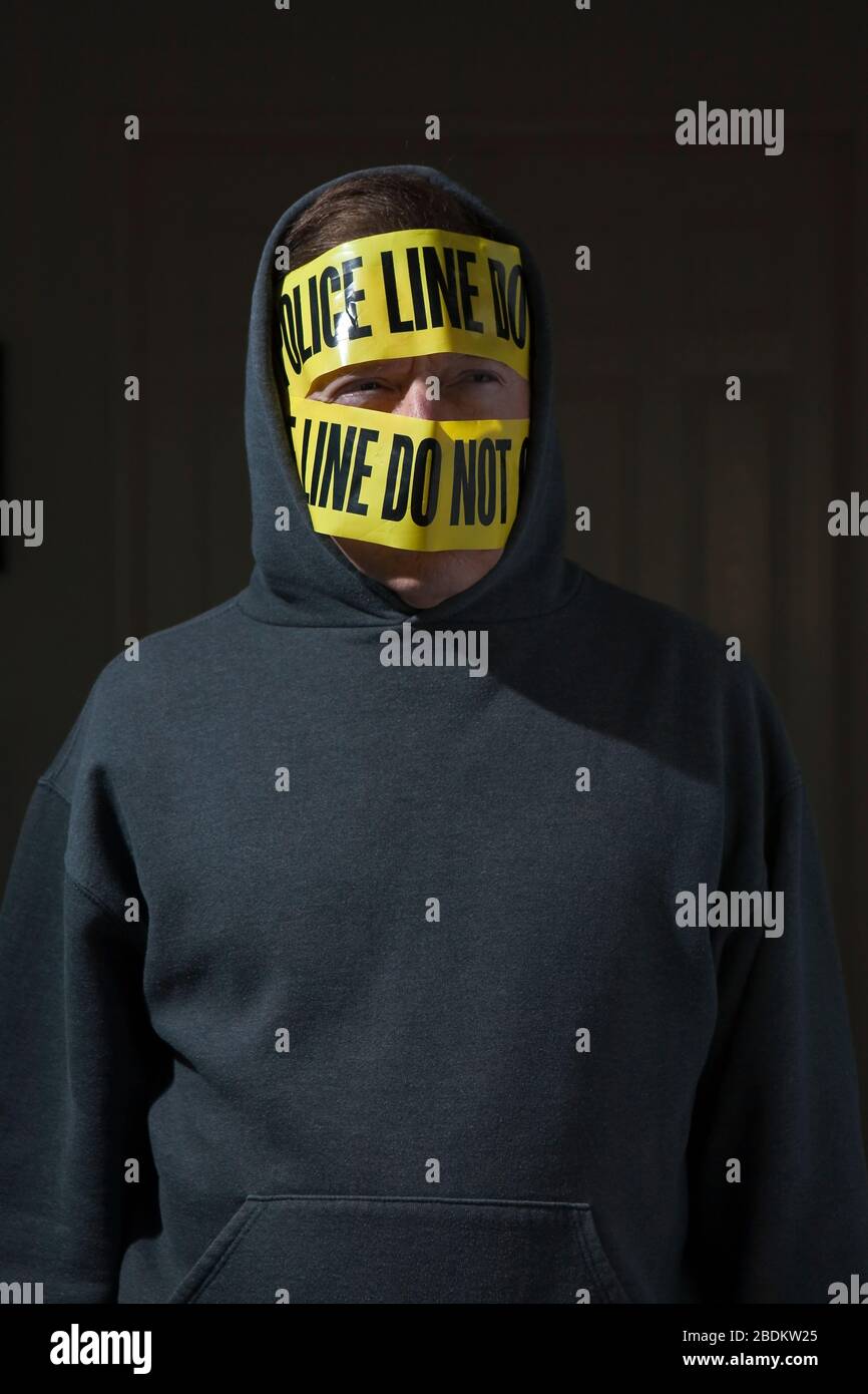 Man in dark hoodie with police crime scene tape around face Stock Photo ...