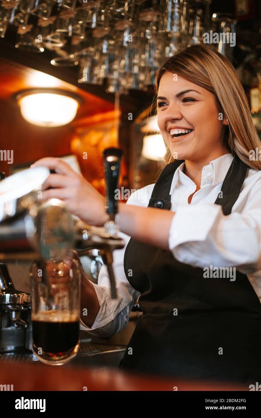 A young attractive blonde caucasian waitress pouring beer in a cafe ...