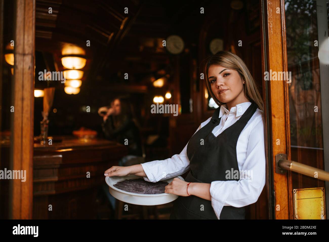 A young attractive blonde caucasian waitress with a tray in a cafe ...