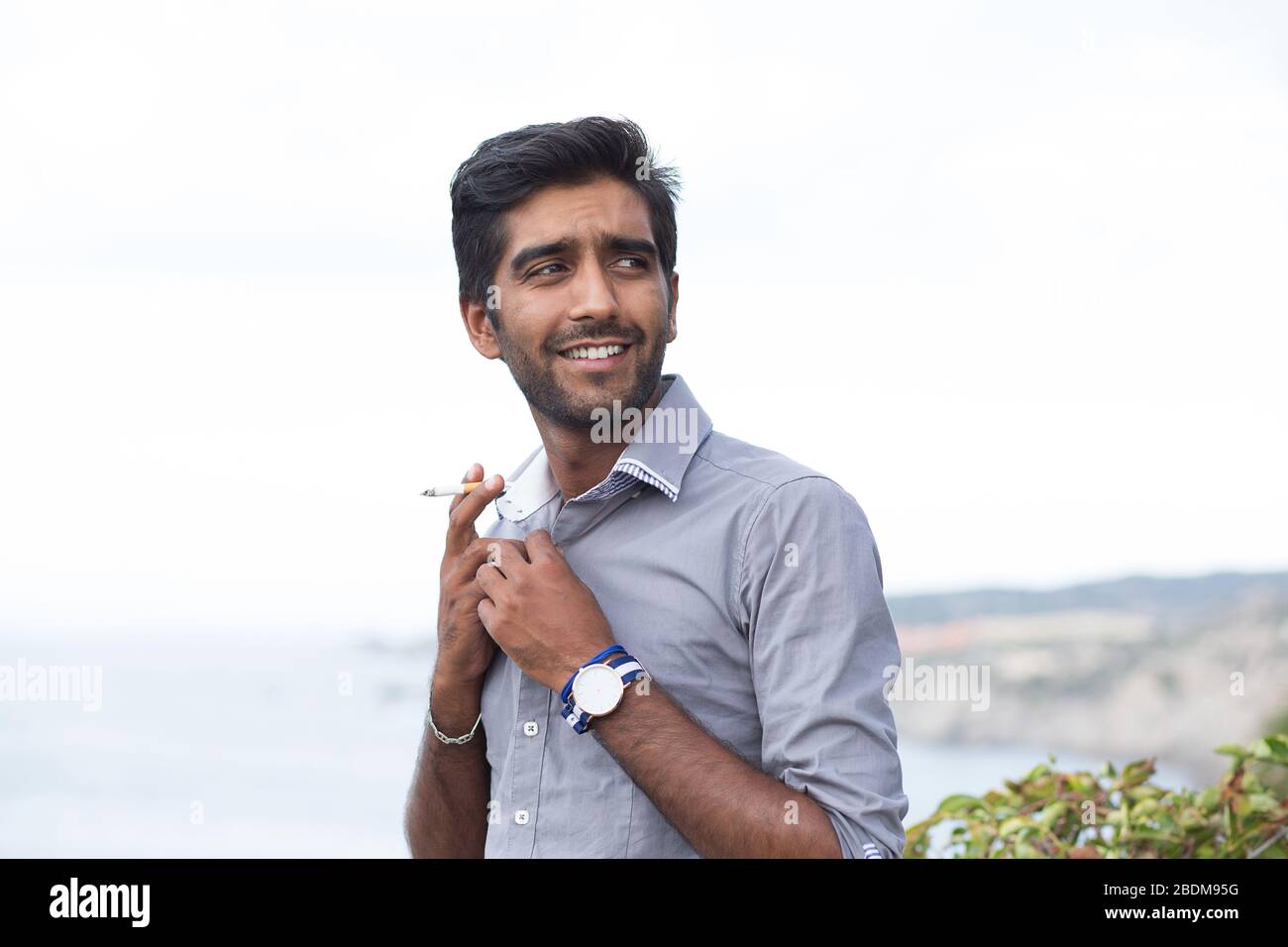 Happy ethnic man smoking cigarette, smiling, thinking looking sidewards ...