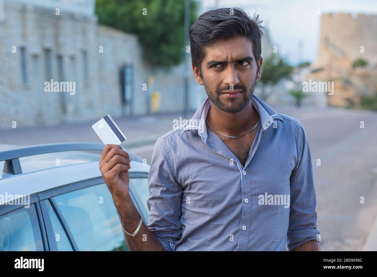 Indian young man holding showing credit card standing next to his car ...