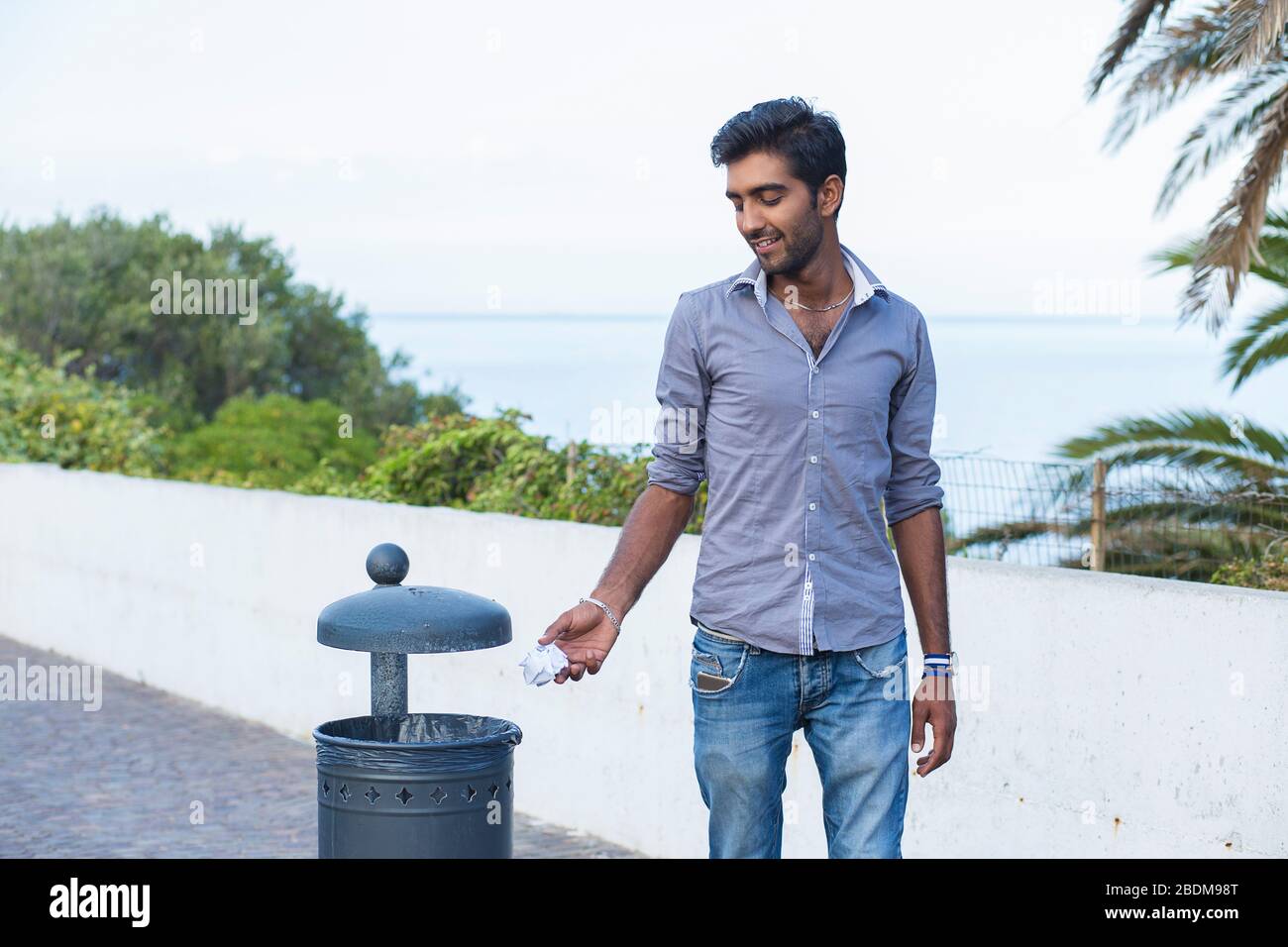 Man throwing trash in recycling bin, isolated outside seaside tropical ...