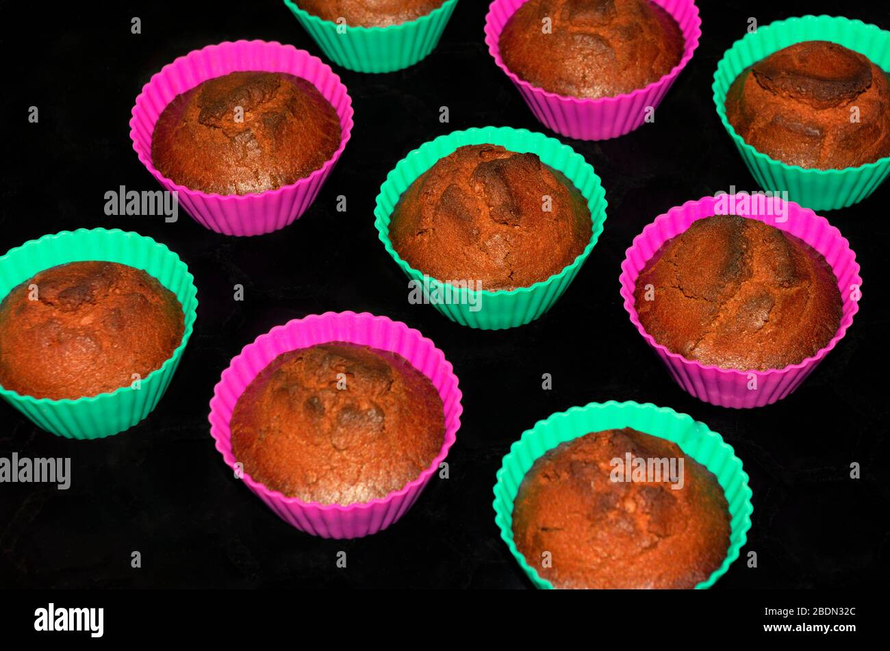 Nine freshly baked muffins in purple and green cups on a black ...
