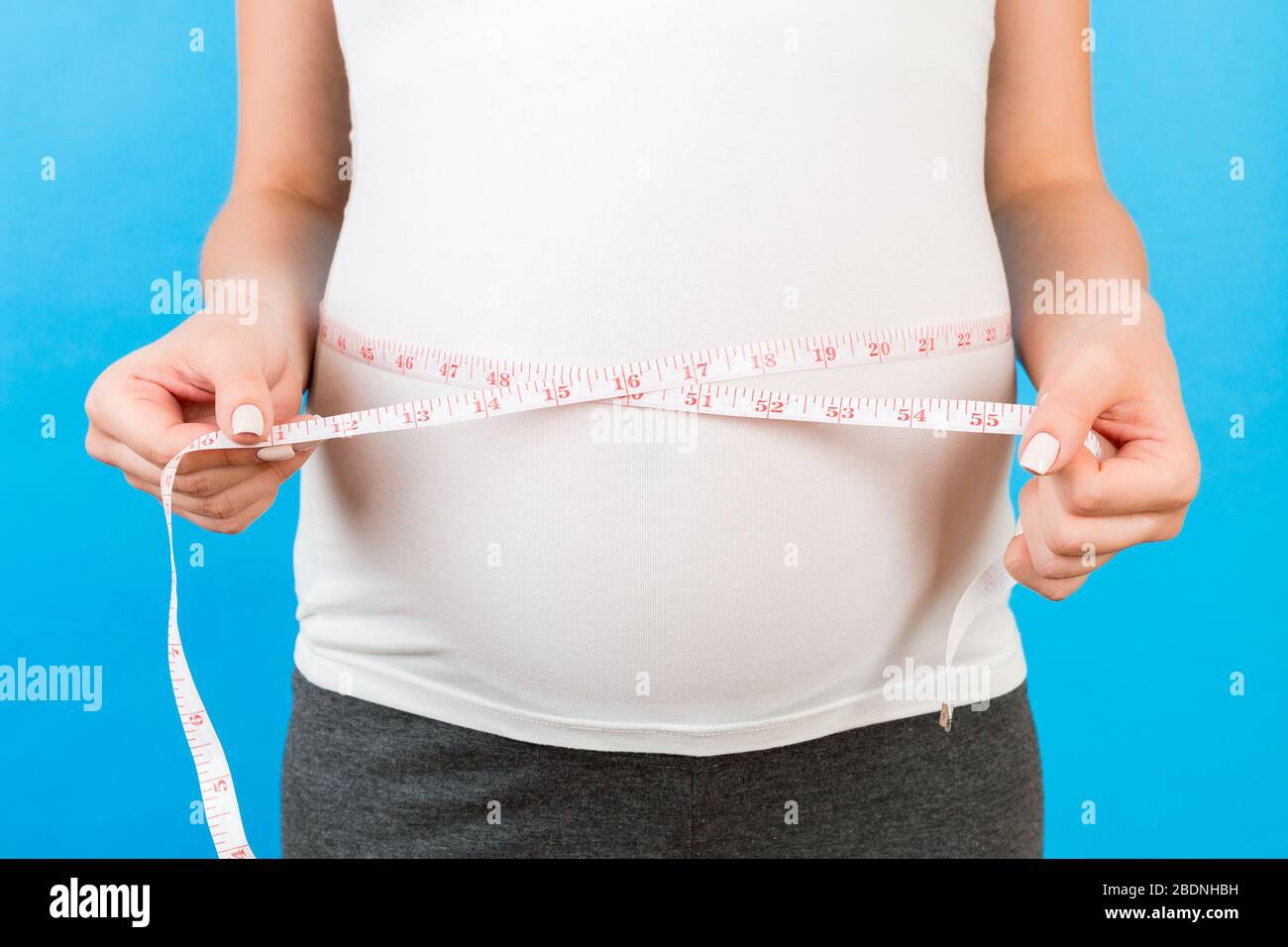 Cropped image of pregnant woman in home clothing measuring her growing ...