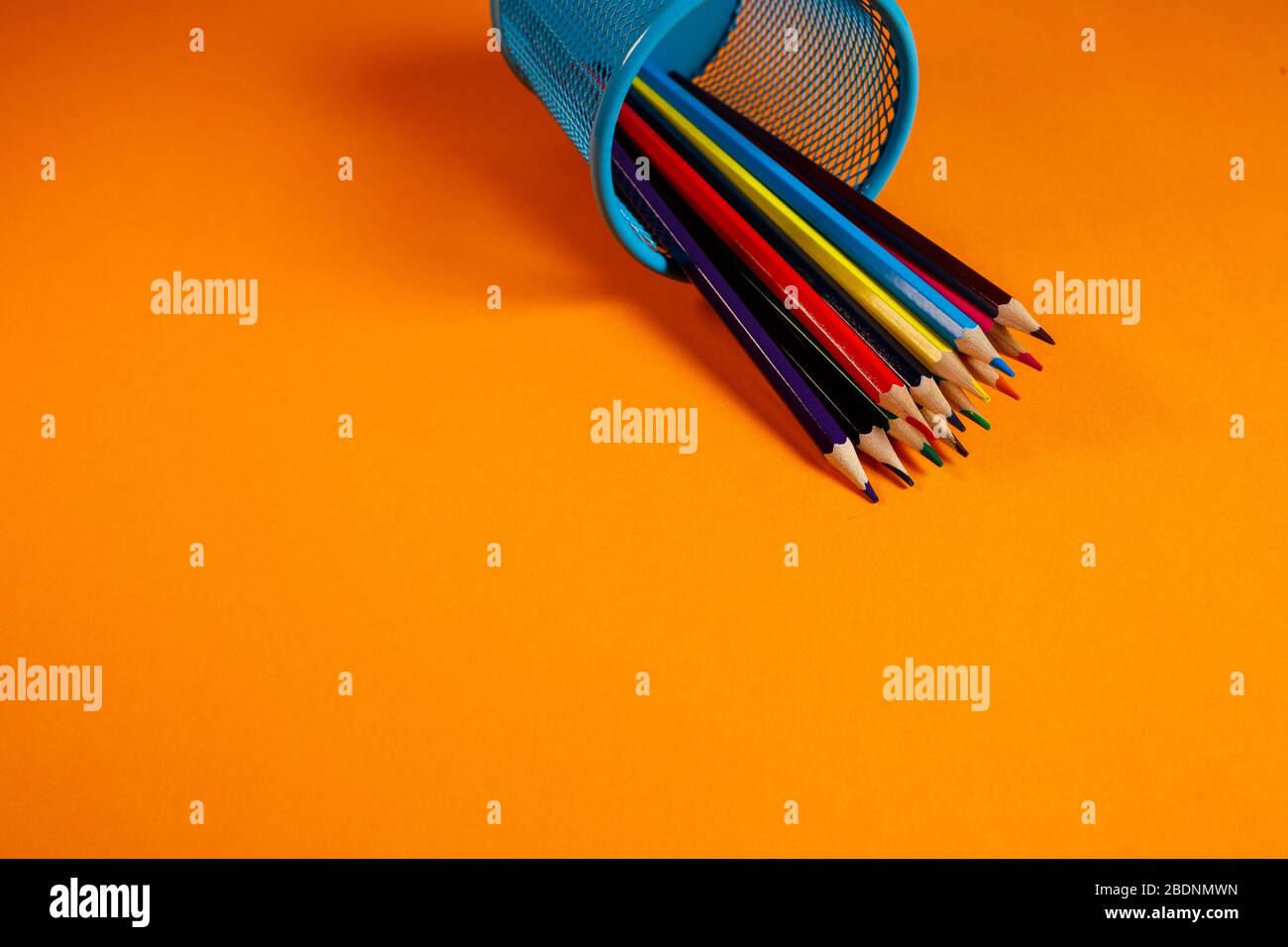 blue metal bucket with colored pencils for office on an orange ...