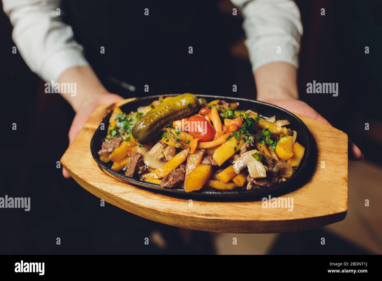 Cooked hot meat with vegetables in a frying pan in the hands of the ...