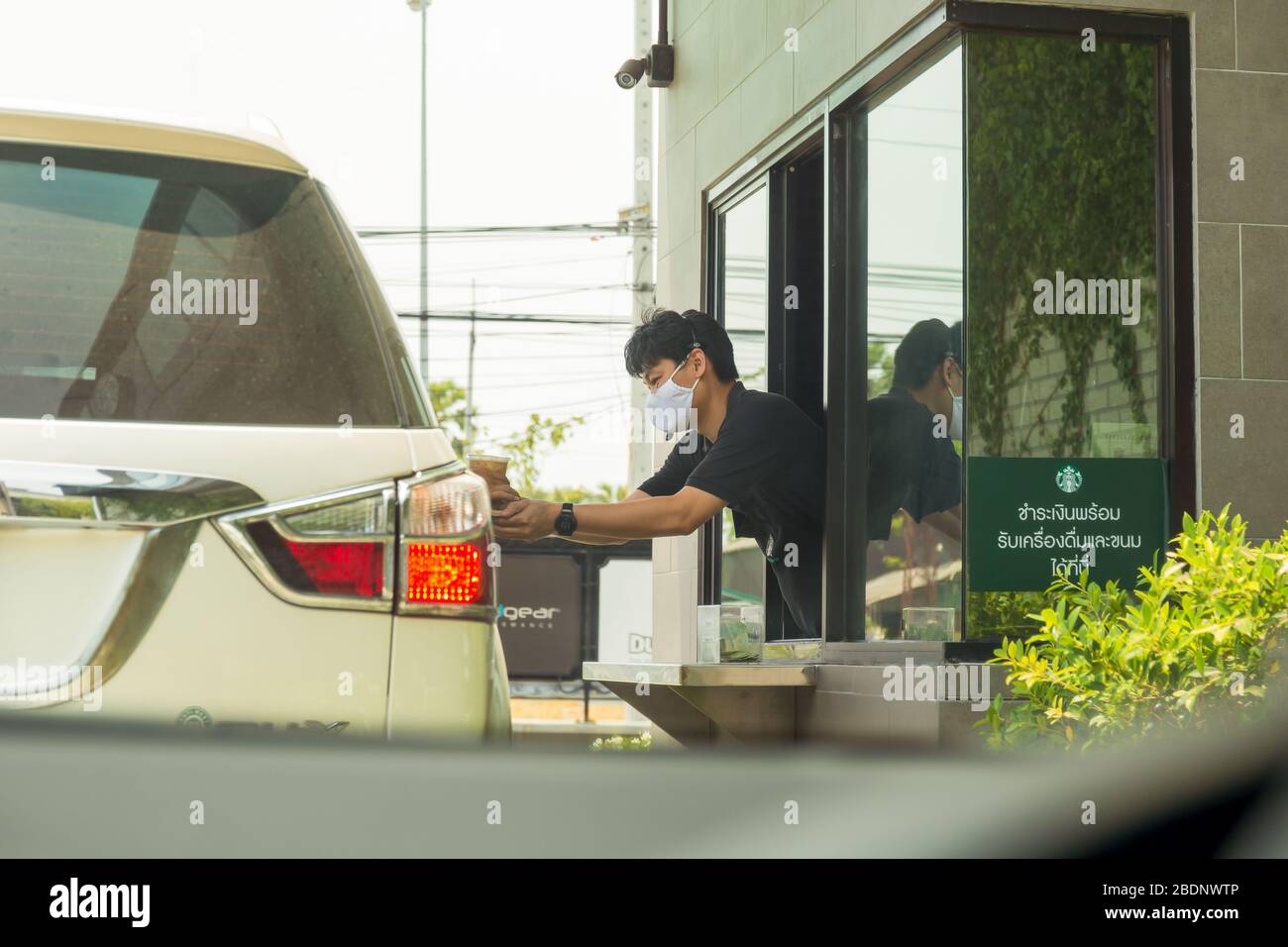 Staff with protective mask serving coffee to customer at drive thru ...