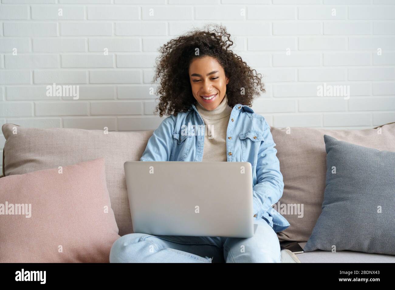 Happy african teen girl using laptop computer sitting on sofa Stock ...