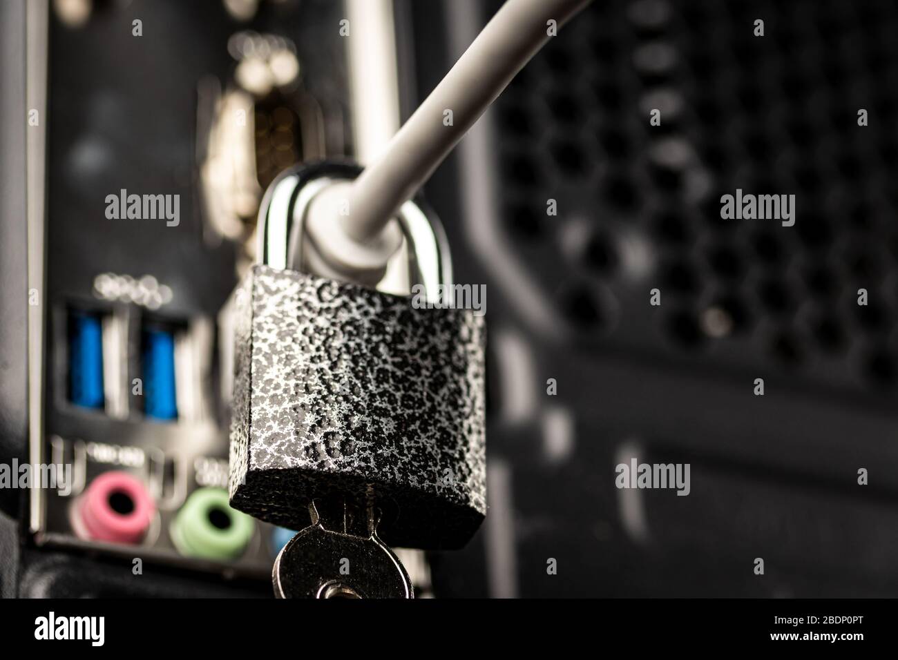 Closed lock with key hanging on a network cable plugged into a computer ...