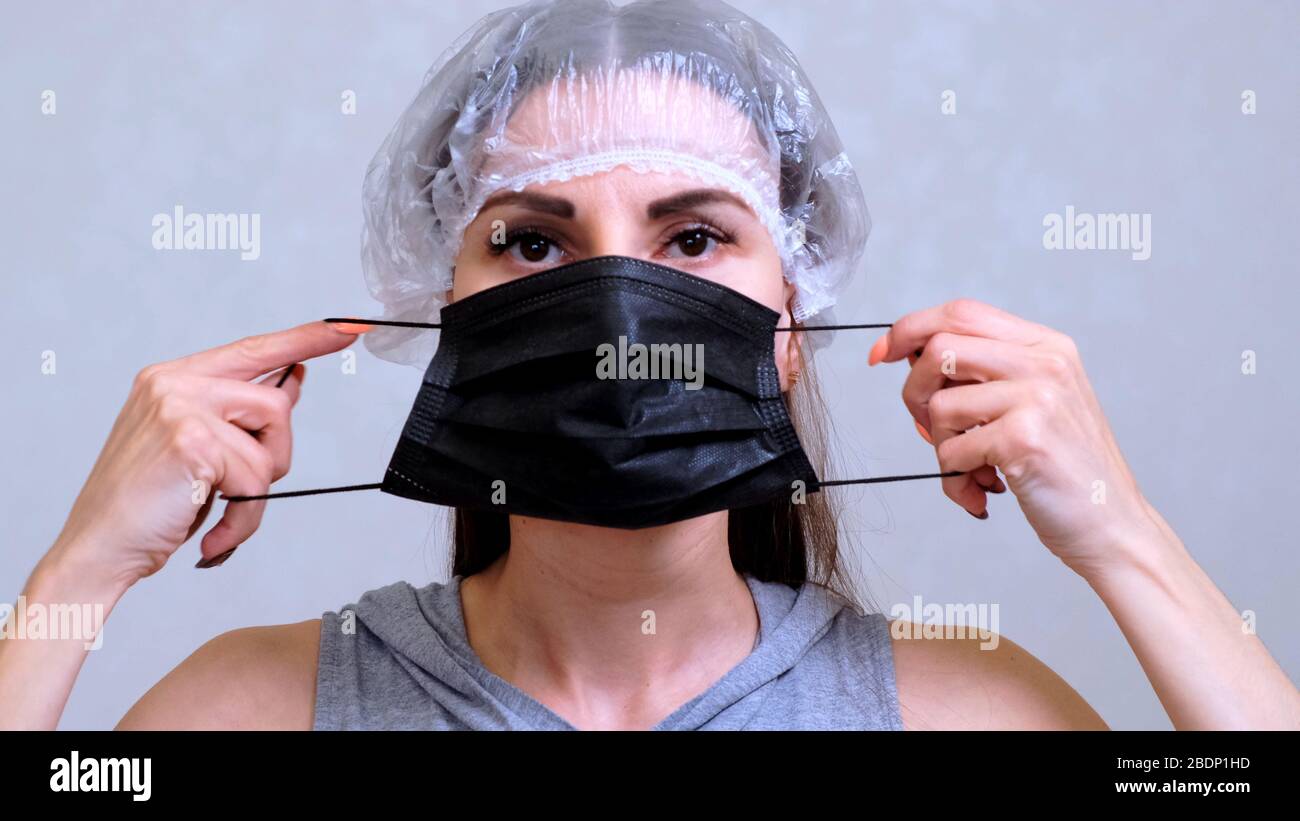 Female patient in a disposable cap puts on a black protective mask ...