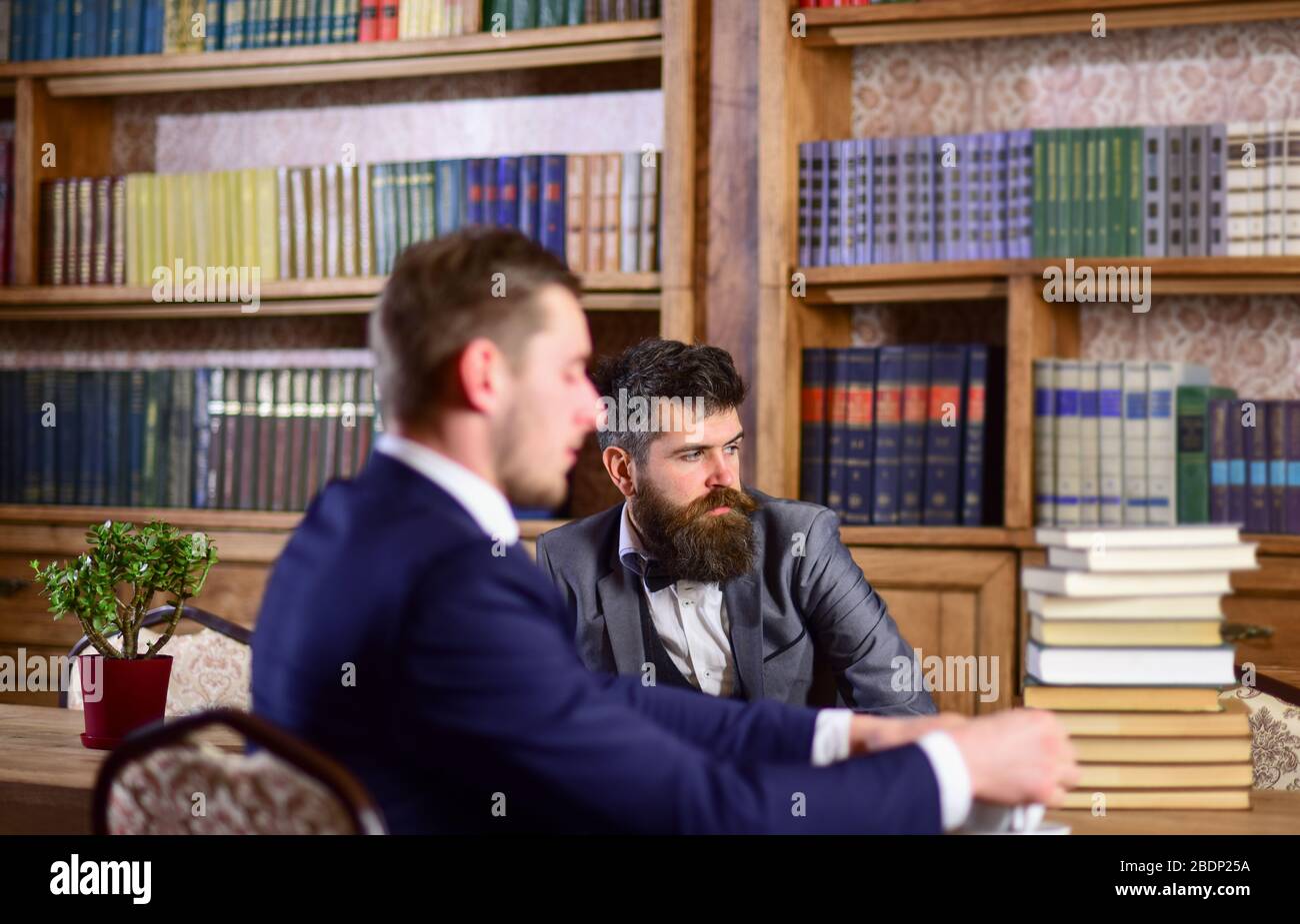 Men with serious faces in retro interior with bookshelves on background ...