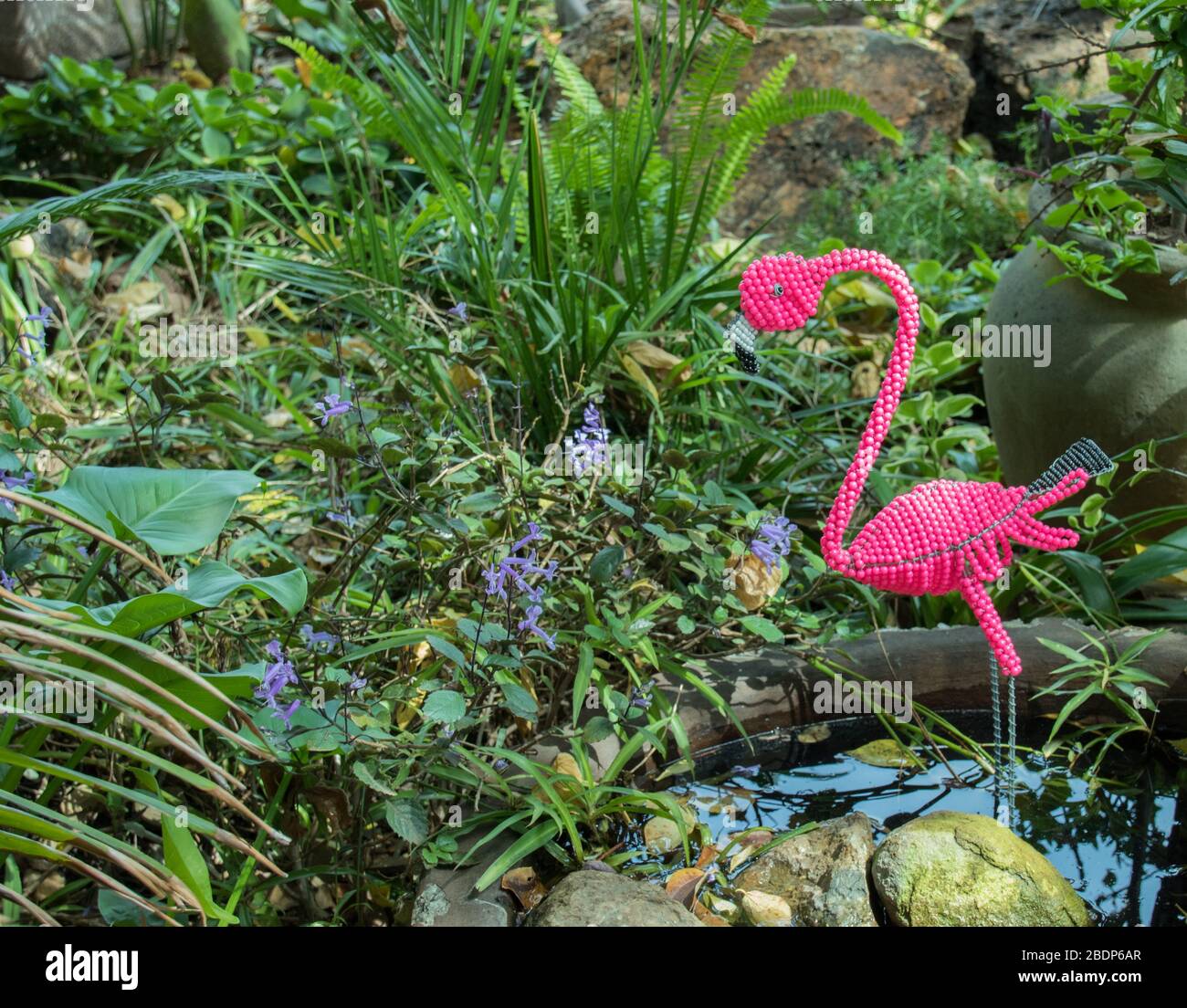 Fake pink flamingo stands isolated in a small pond in the garden ...
