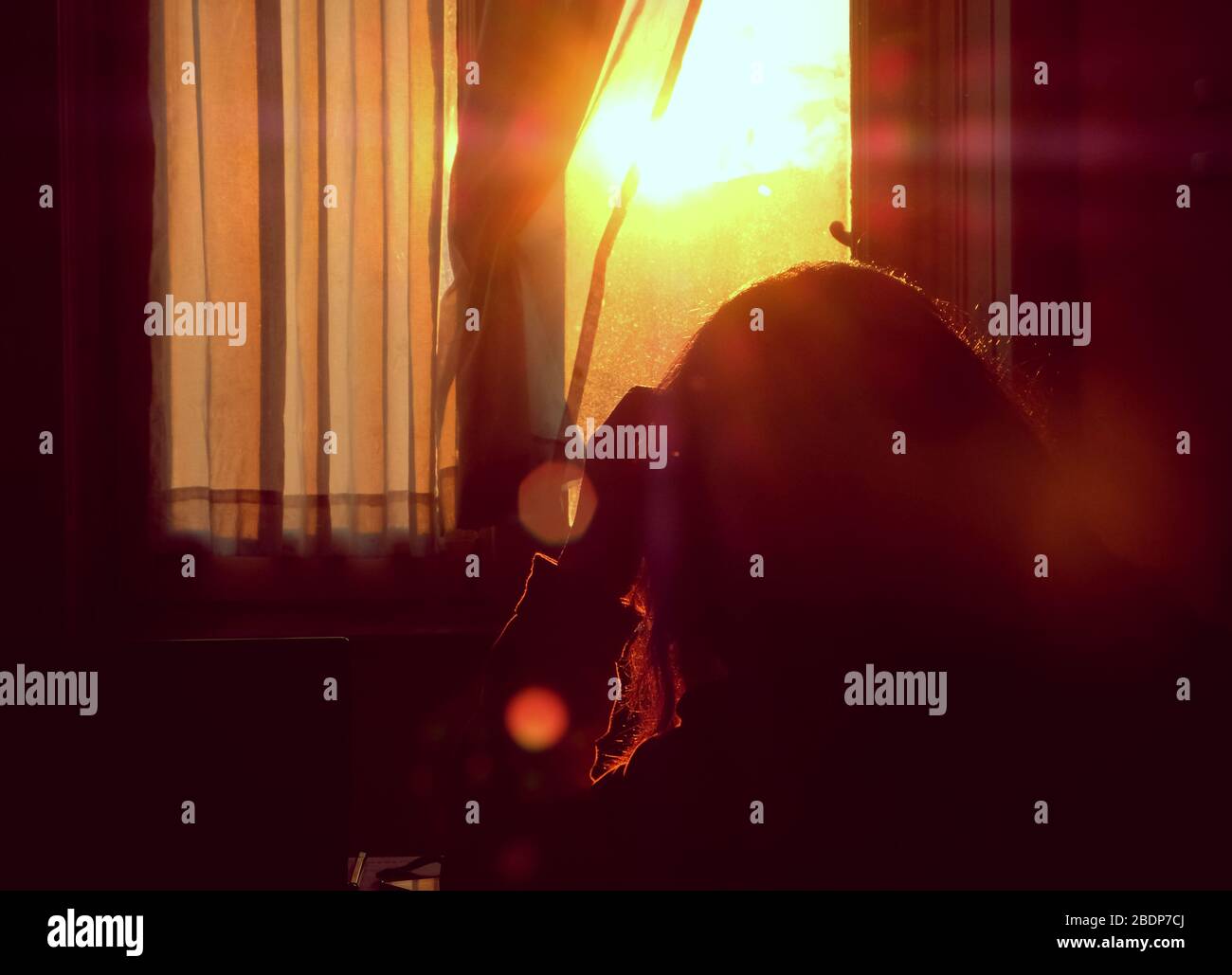 sad woman or girl in her room in front of the window during sunset ray ...