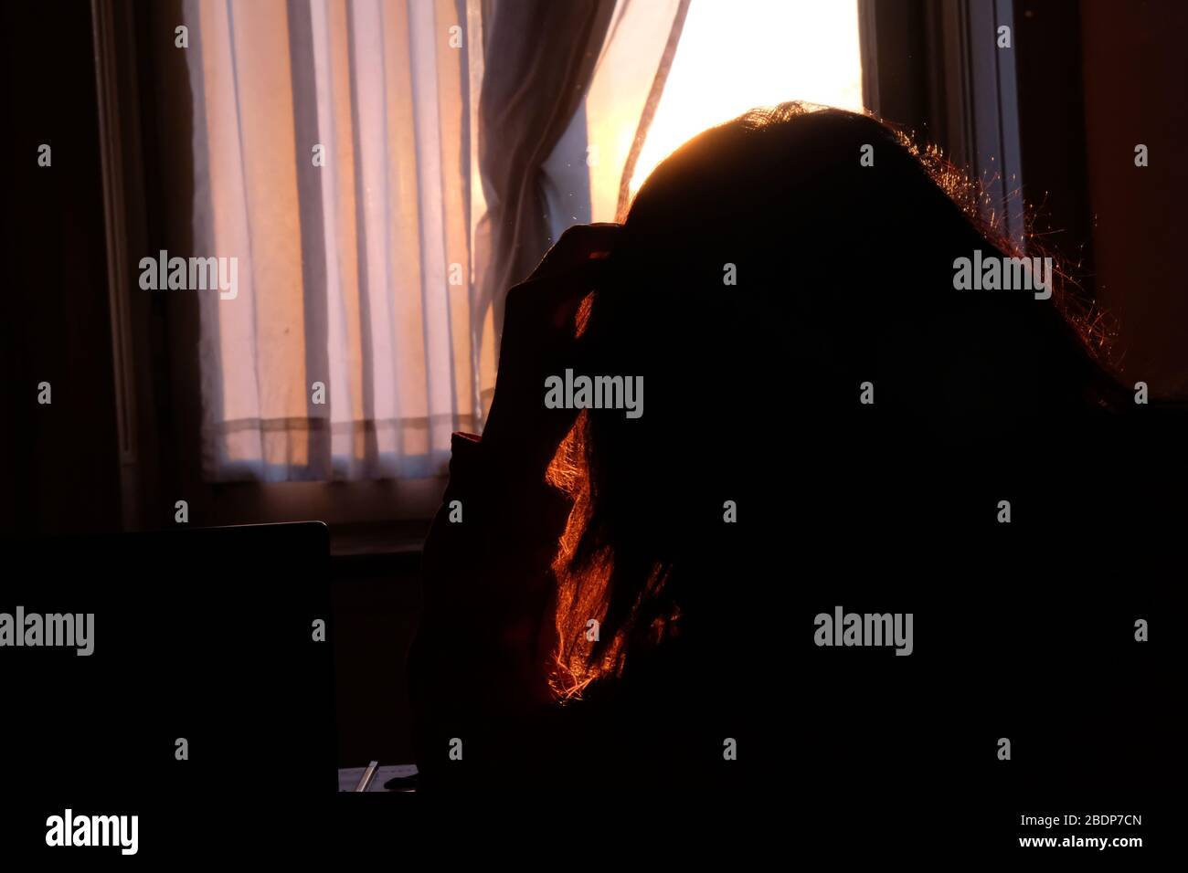 sad woman or girl in her room in front of the window during sunset ray ...