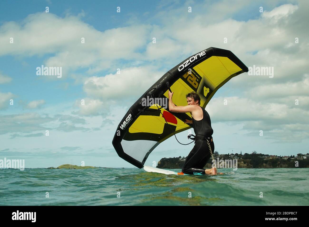 A man wingfoils in Auckland Harbour on a summer's day, using a hand ...