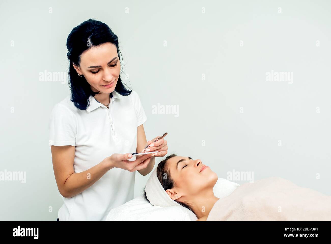 Cosmetologist and patient while eyelash extension procedure on white ...