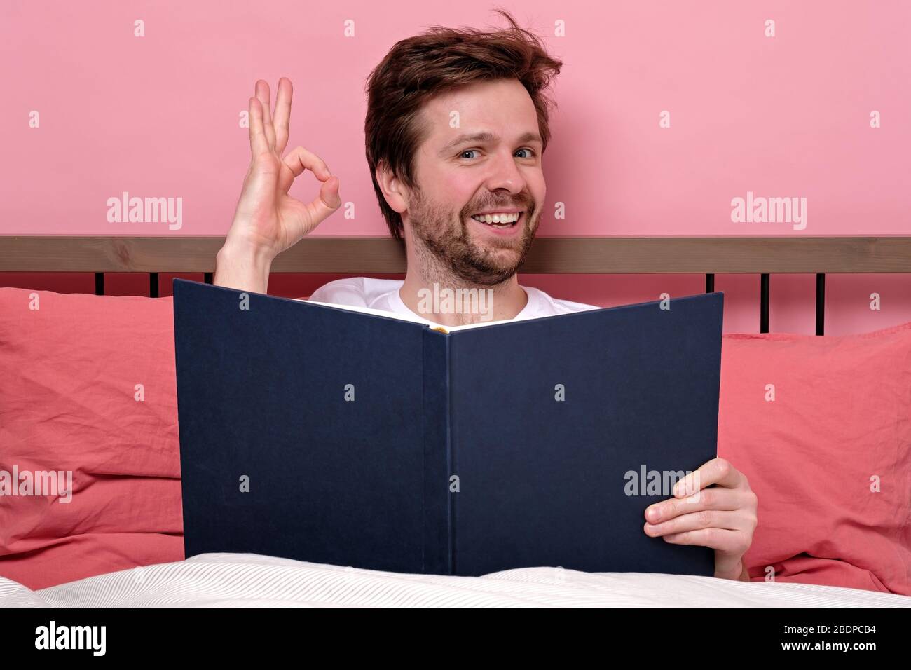 Reading an exciting book sitting on bed at home. Man reading the book ...