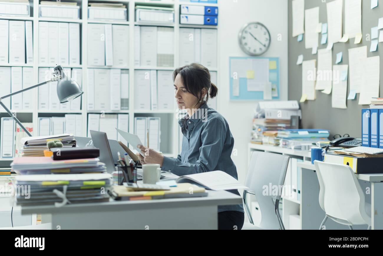Efficient female office clerk sitting at desk in the office and working ...