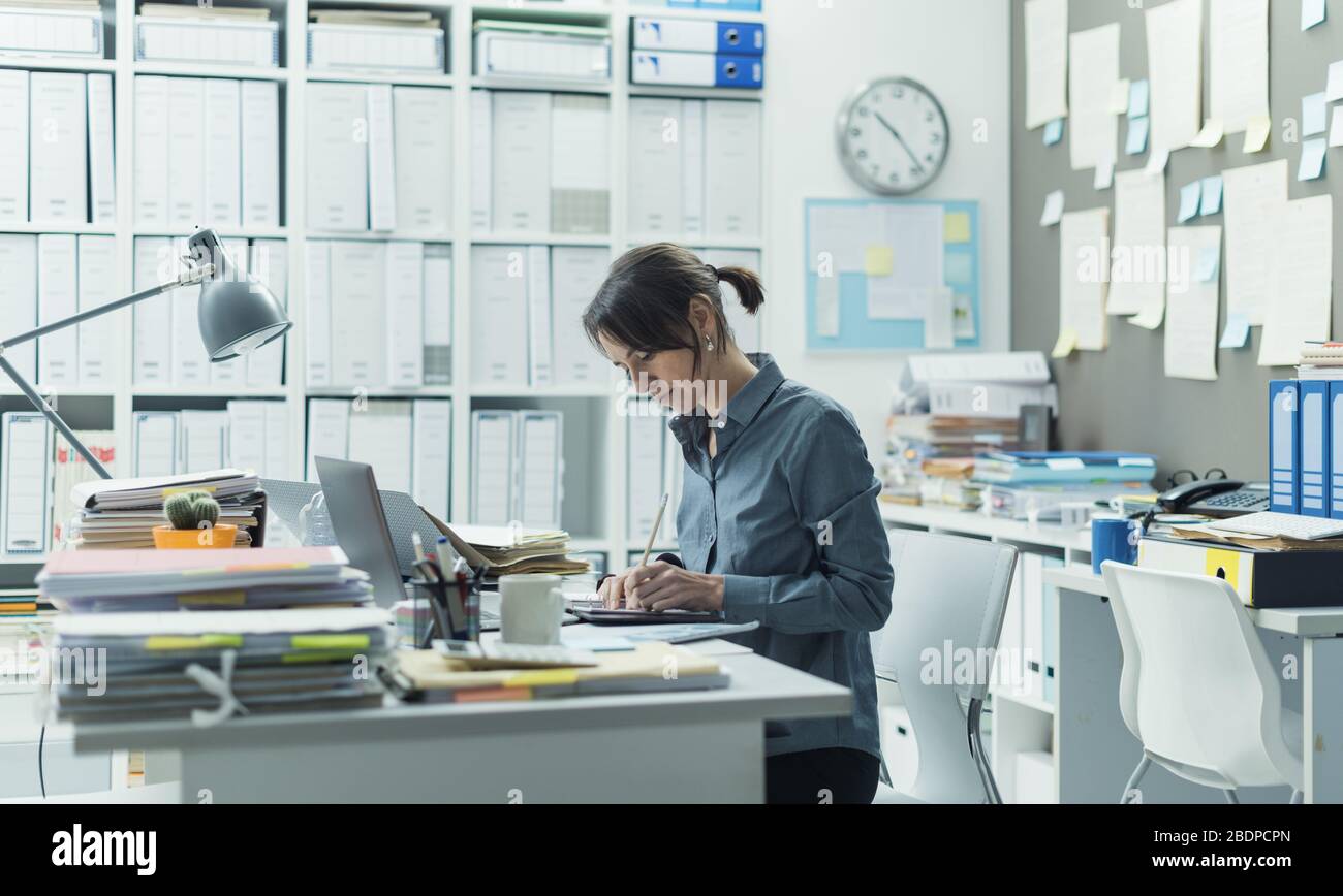 Confident businesswoman working in the office, she is writing notes on ...