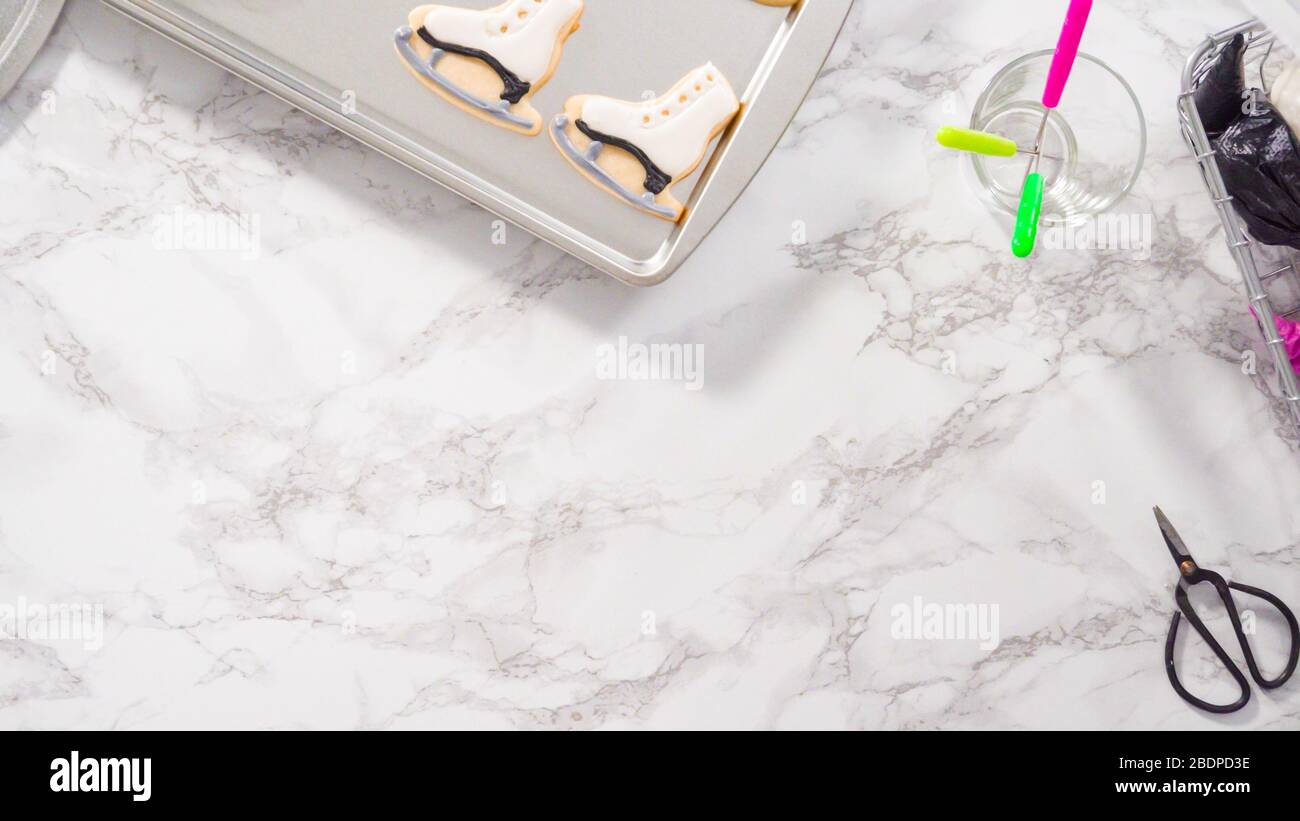 Flat lay. Decorating ice skate shaped sugar cookies with black color ...