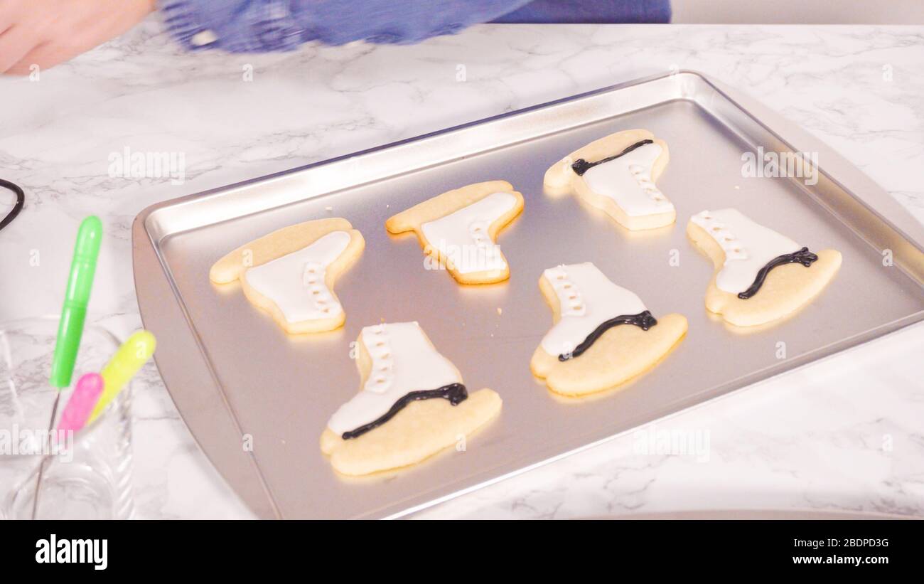 Decorating ice skate shaped sugar cookies with black color royal icing ...