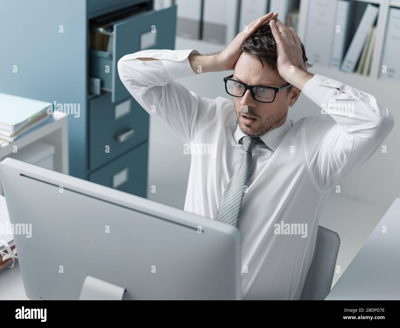 Panicking businessman with head in hands in his office, he is receiving ...