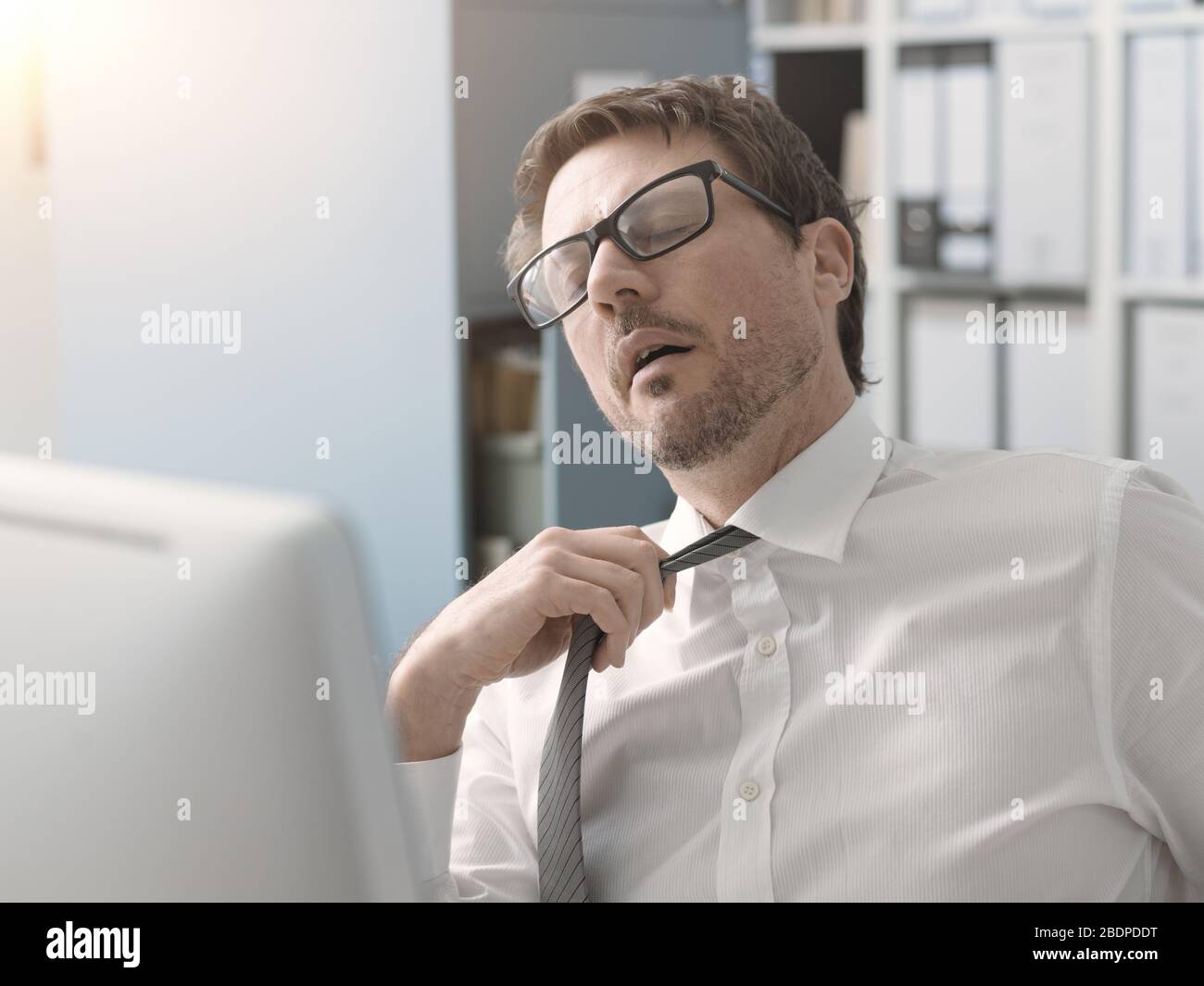 Stressed business executive working at office desk, he is feeling hot ...