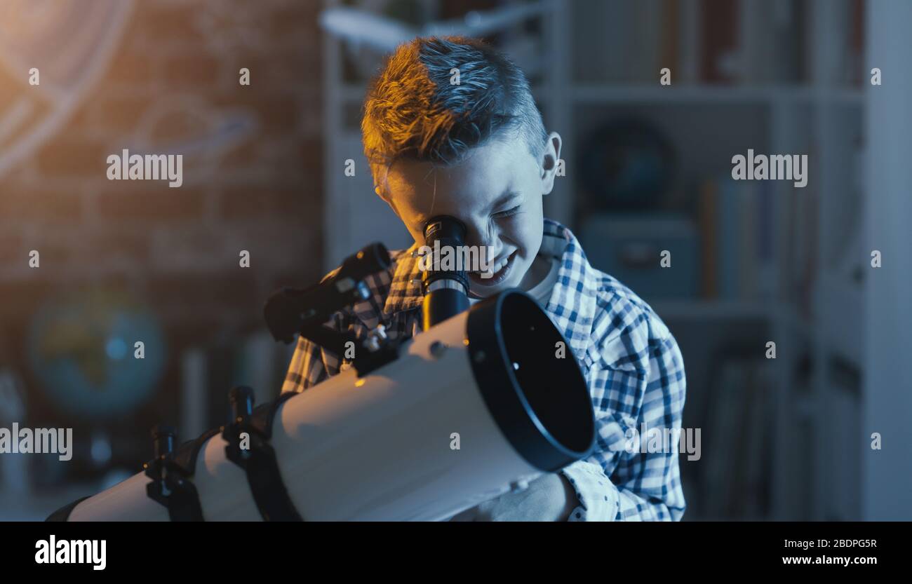 Cute boy watching stars through a telescope at night in his bedroom ...