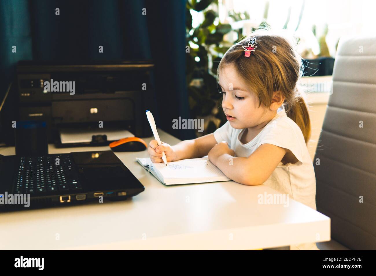 Little cute girl sit at the table and write in notebook. Learning at ...
