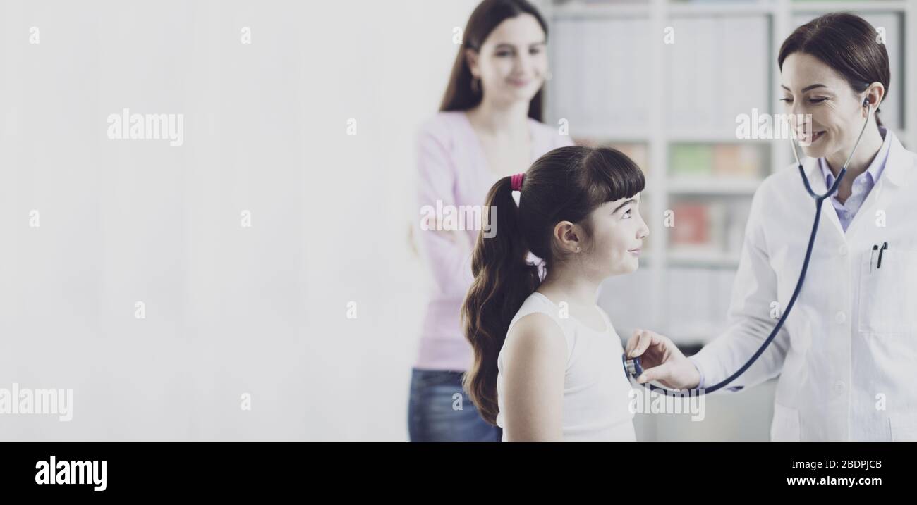 Female doctor examining a cute smiling girl with a stethoscope, the ...