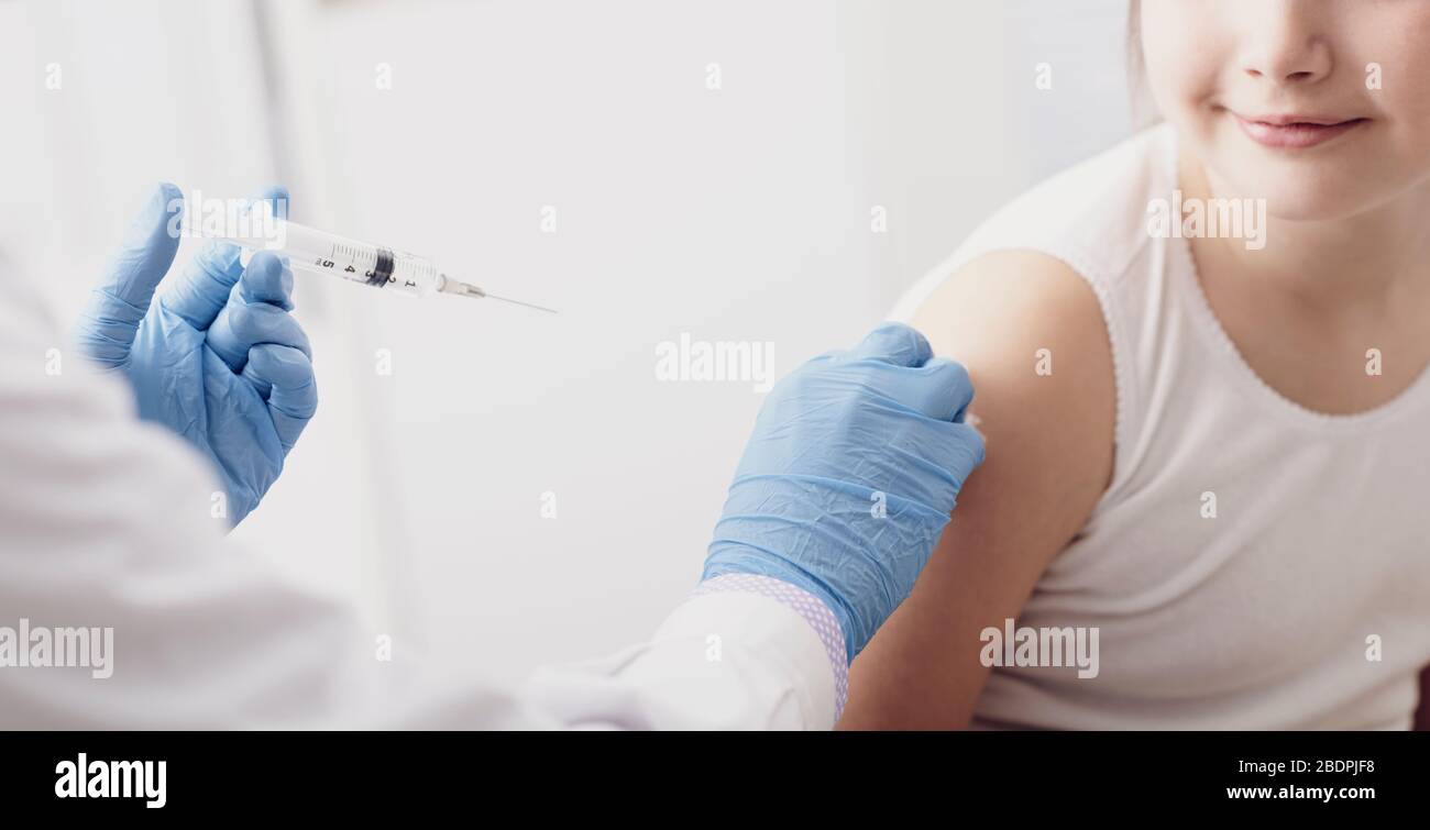 Doctor giving an injection to a young patient, the girl is smiling and ...