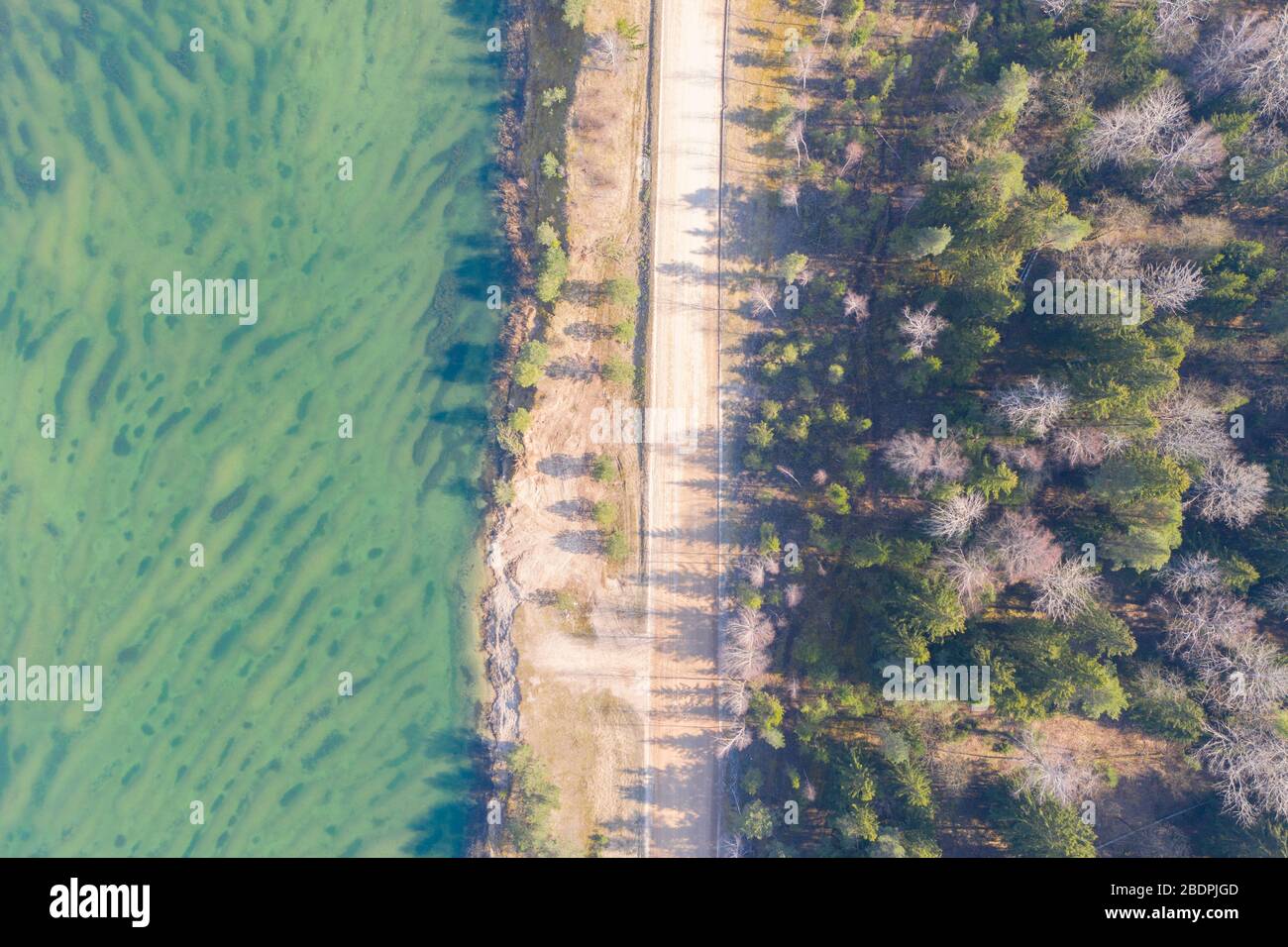 Aerial top down view of gravel road between green water and forest ...