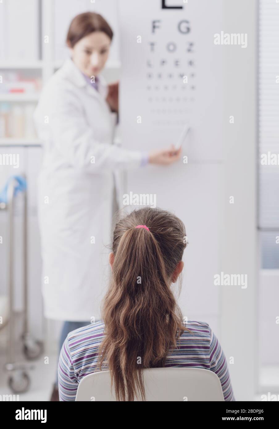 Oculist testing a young patient's eyesight using an eye chart ...