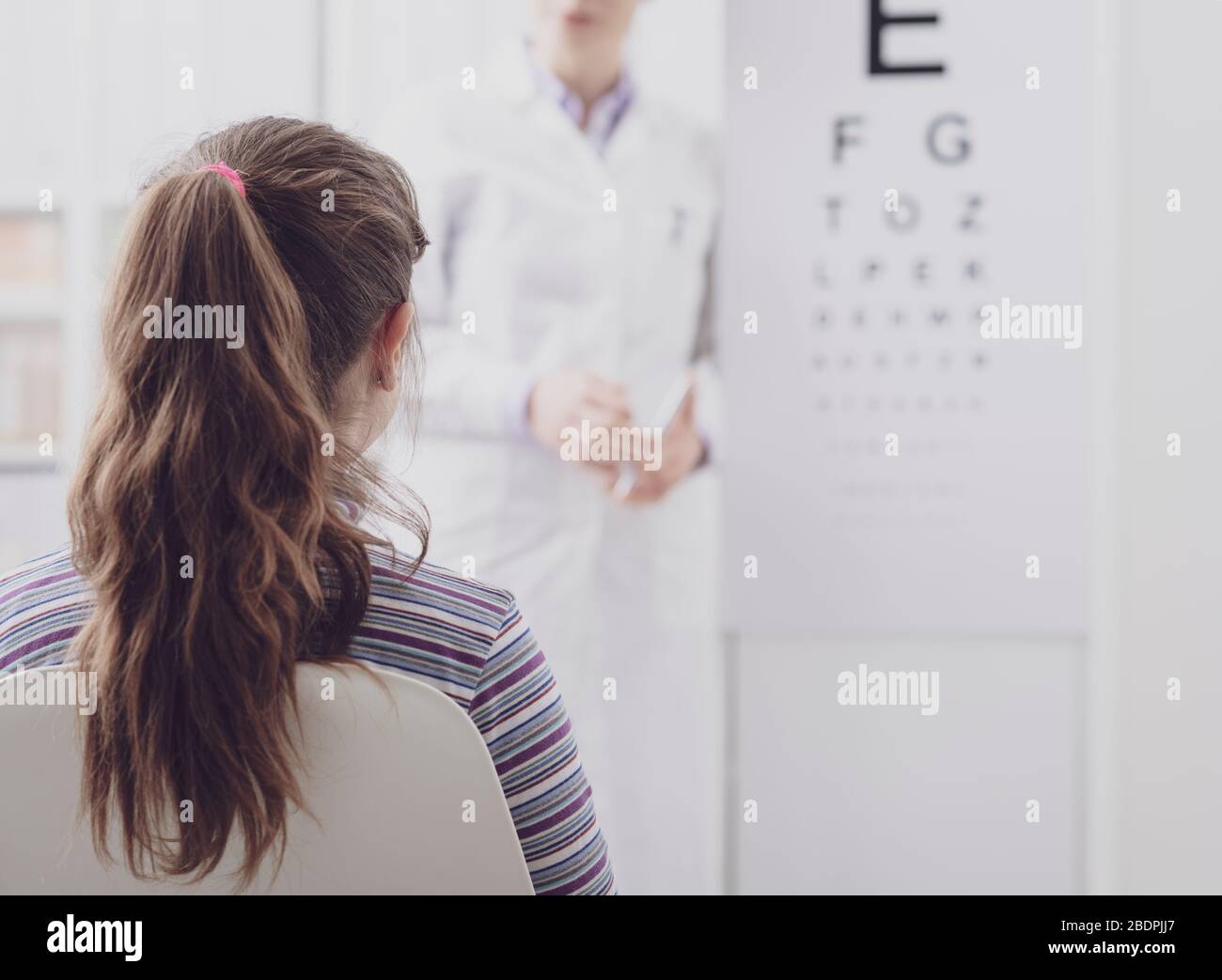 Oculist testing a young patient's eyesight using an eye chart ...